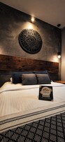 Quarto de hotel moderno com uma cama grande, cabeceira de madeira, relógio de parede e um aviso de boas-vindas.