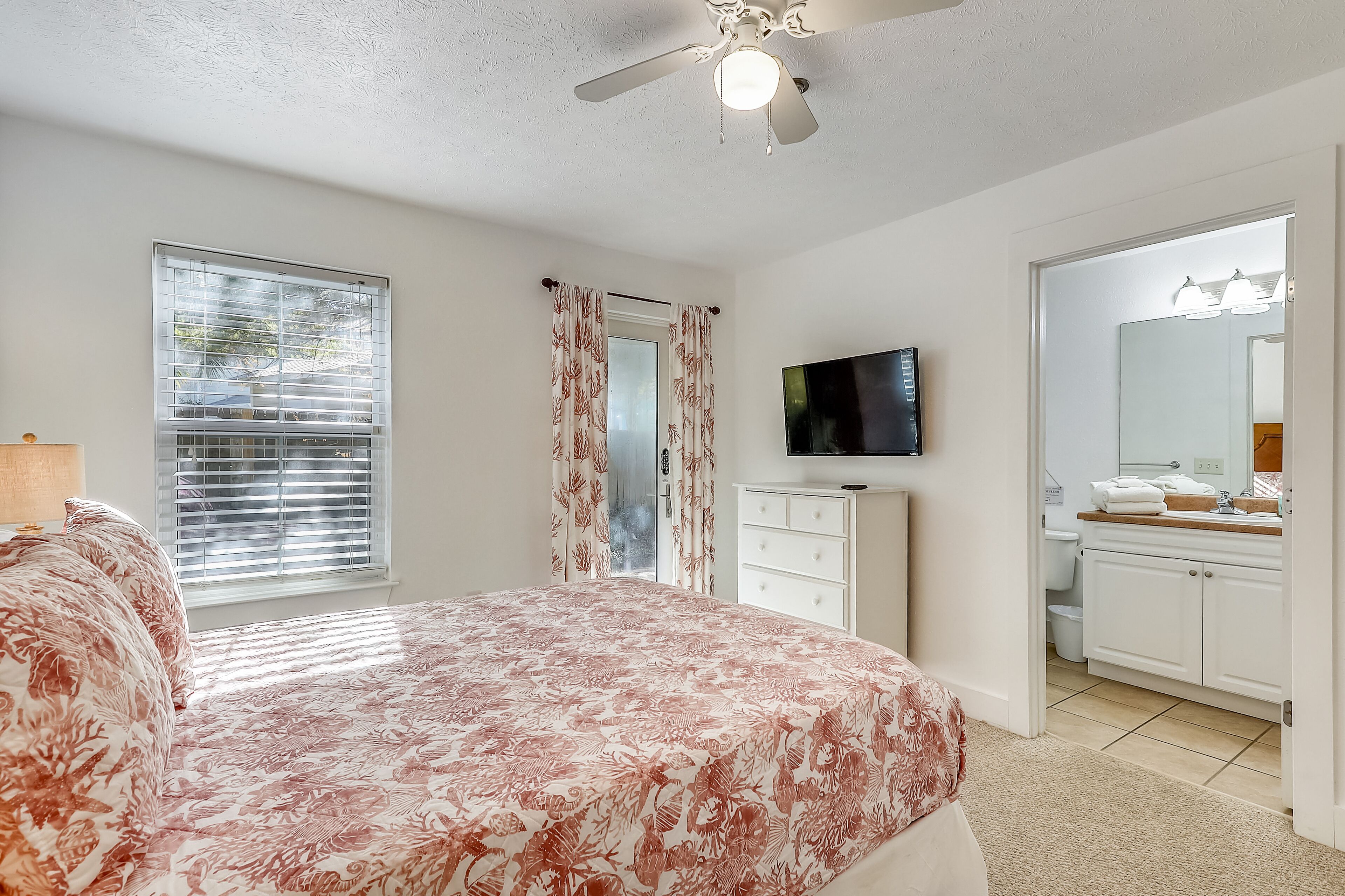 Quarto com cama, televisão, cômoda e banheiro visível por uma porta aberta.
