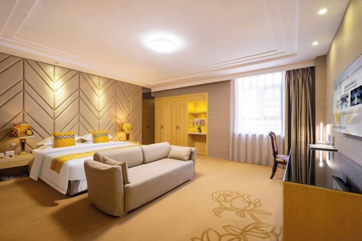 Quarto de hotel com cama, sofá, escrivaninha e uma grande janela com cortinas.