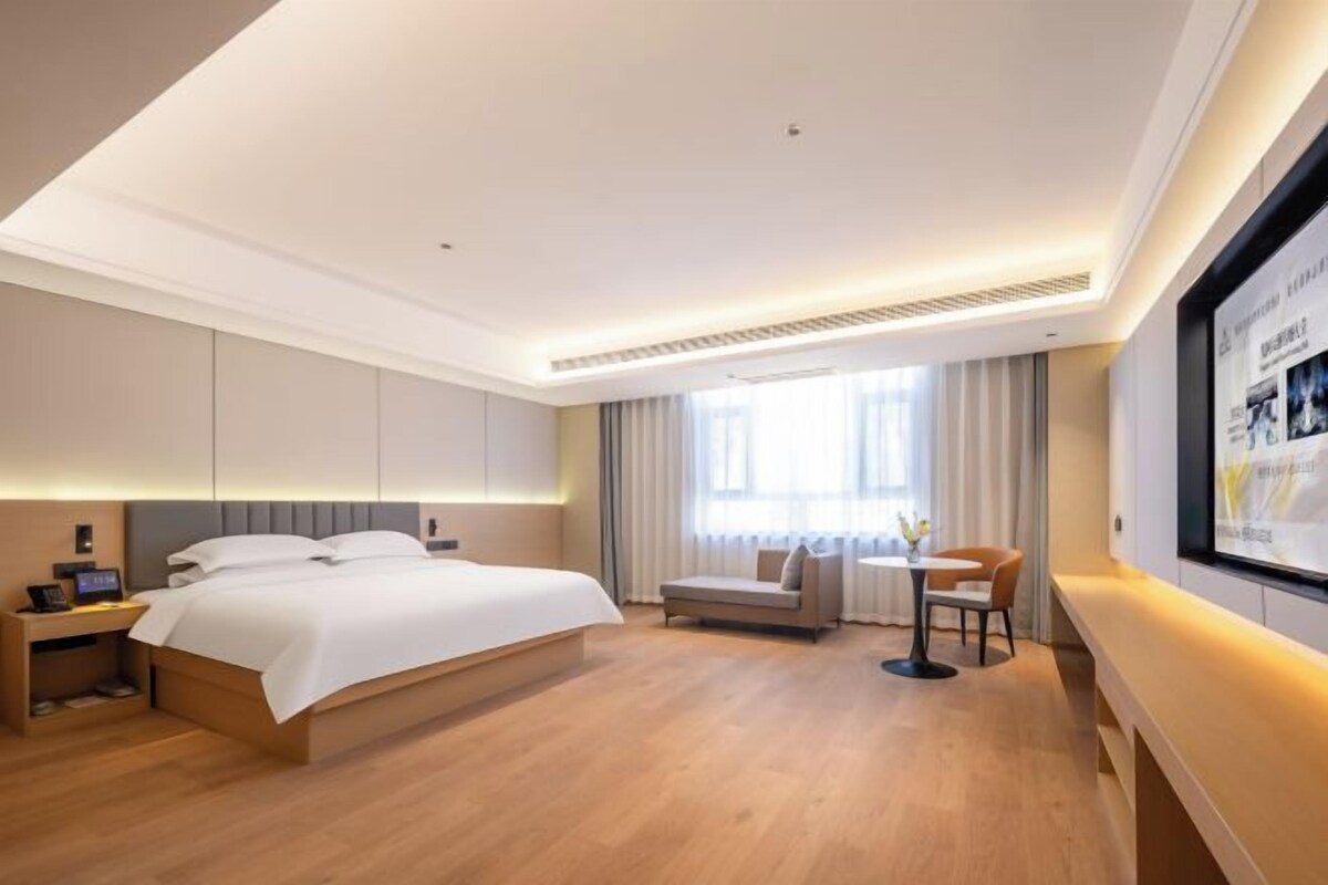 Quarto de hotel moderno com uma cama grande, um sofá pequeno, uma escrivaninha e uma TV fixada na parede.