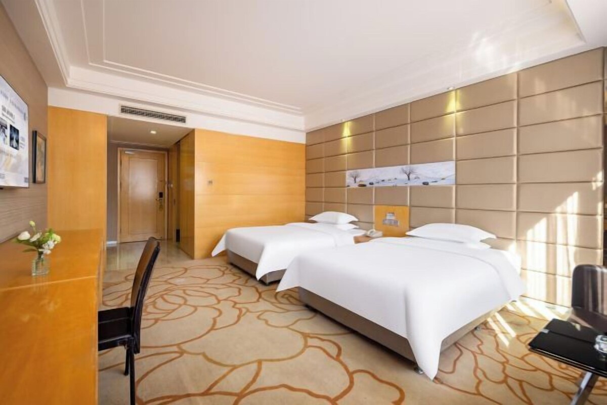 Quarto de hotel com duas camas, uma escrivaninha e uma cadeira.