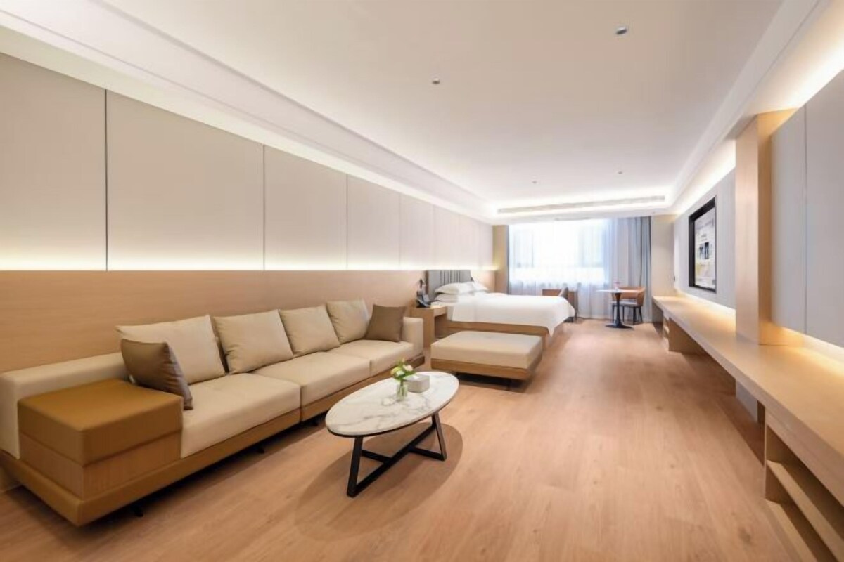Quarto de hotel moderno com sofá, cama, mesa pequena e escrivaninha.