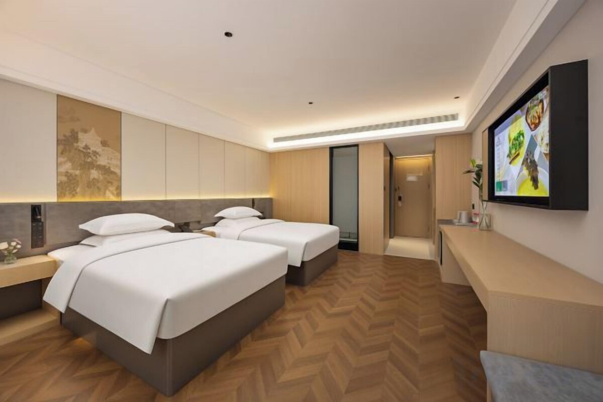 Quarto de hotel com duas camas, televisão e piso de madeira em padrão herringbone.