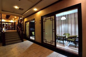 Um saguão de hotel com escadaria, balcão de recepção e vista para a área de estar externa.