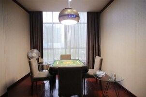 Quarto com mesa, cadeiras, ventilador e janela com cortinas.