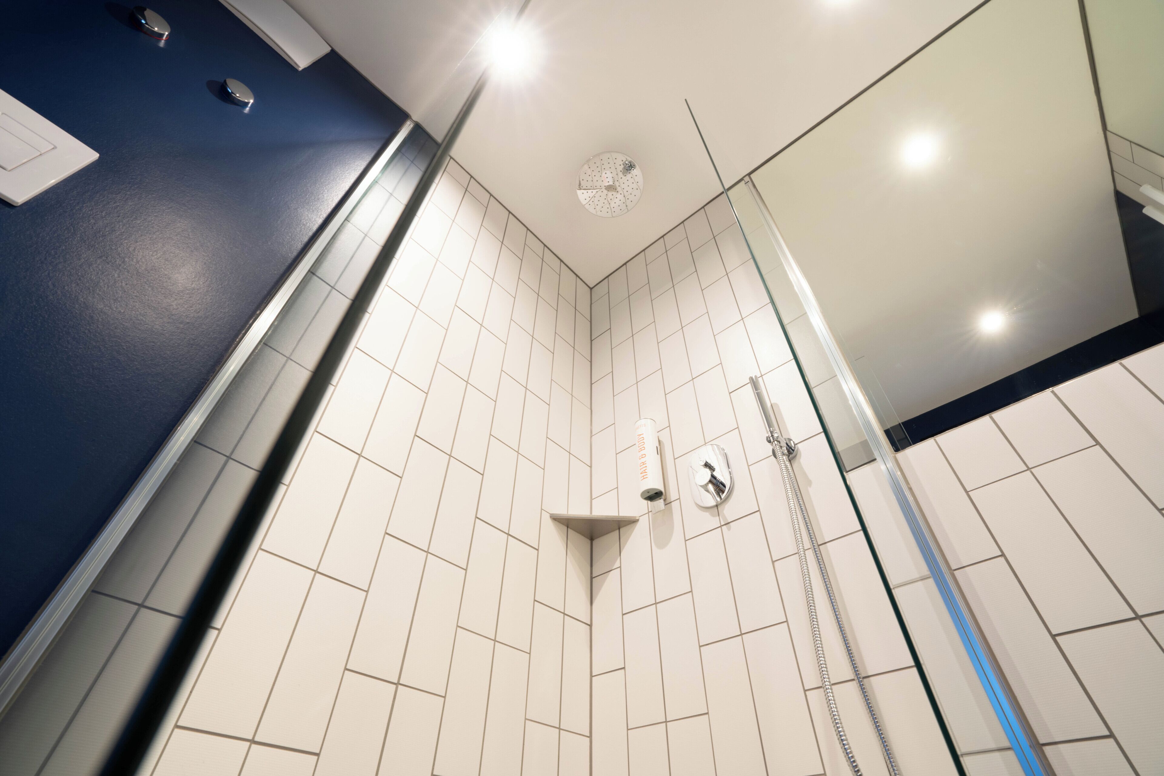 Um banheiro moderno com azulejos brancos, box de vidro e uma parede azul decorativa.