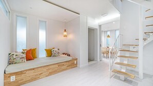 Quarto moderno e claro com uma cama de madeira estilo banco, uma escada com degraus de madeira e uma área de jantar ao fundo.