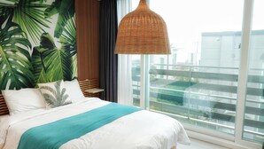 Quarto moderno com uma cama grande, vista da cidade através de amplas janelas e plantas tropicais.