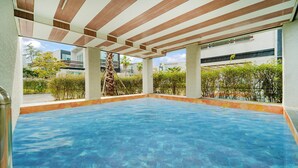 Piscina com teto de madeira e vista para edifícios e vegetação ao redor.