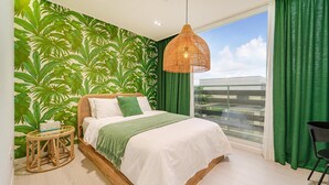 Quarto com cama, mesa de cabeceira de vime, luminária pendente e vista para um edifício através da janela.