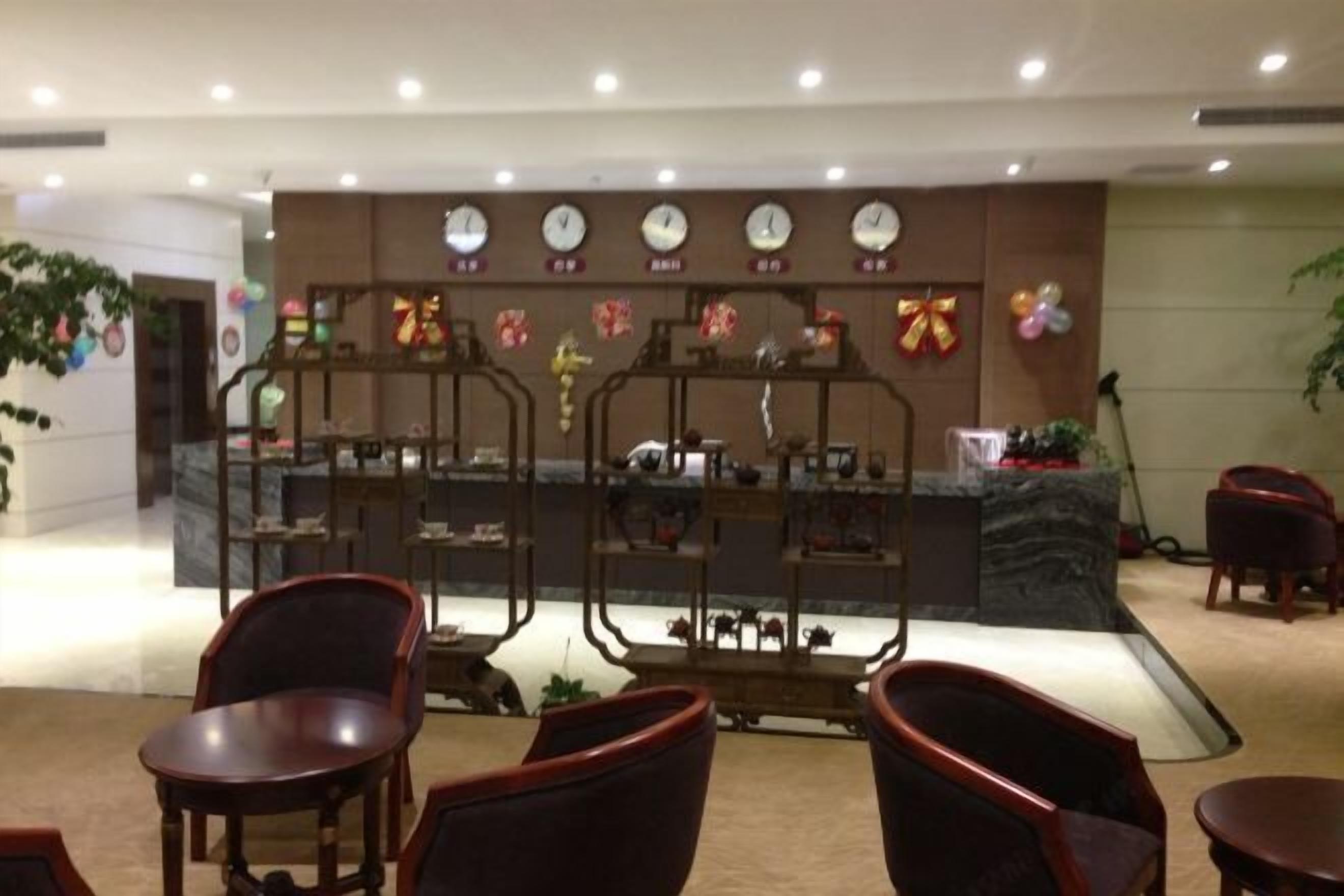 Um saguão com balcão de recepção, cadeiras e uma parede decorativa com relógios e flores.