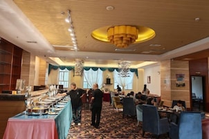 Uma sala de jantar de hotel com uma longa mesa de buffet, várias mesas e cadeiras.
