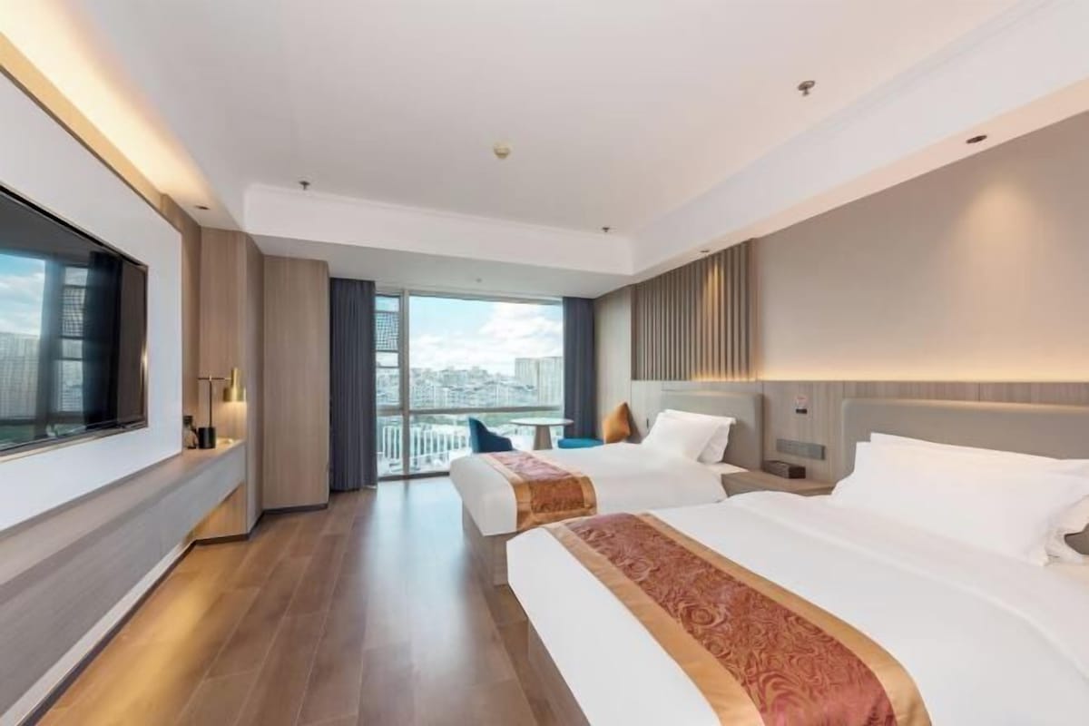 Quarto de hotel moderno com duas camas, uma janela grande com vista para a cidade e uma varanda.