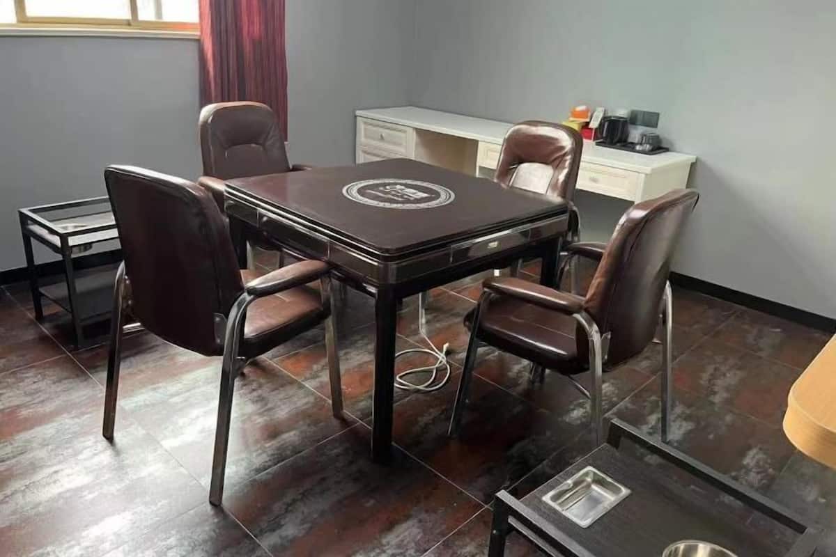 Quarto com uma mesa de madeira escura e quatro cadeiras de couro, uma escrivaninha branca com gavetas e uma pequena mesa lateral com um porta-bandeja de metal.