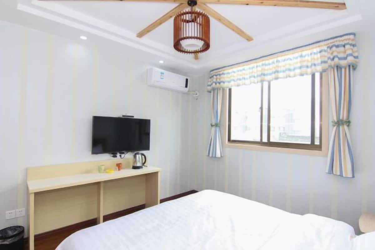 Quarto de hotel com cama, televisão, escrivaninha e janela com cortinas.