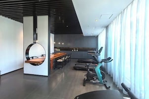 Academia moderna com equipamentos de exercício, área de refeições e grandes janelas.