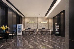 Uma área de recepção moderna com piso de mármore, dois balcões de atendimento, uma máquina de venda automática e iluminação pendente.