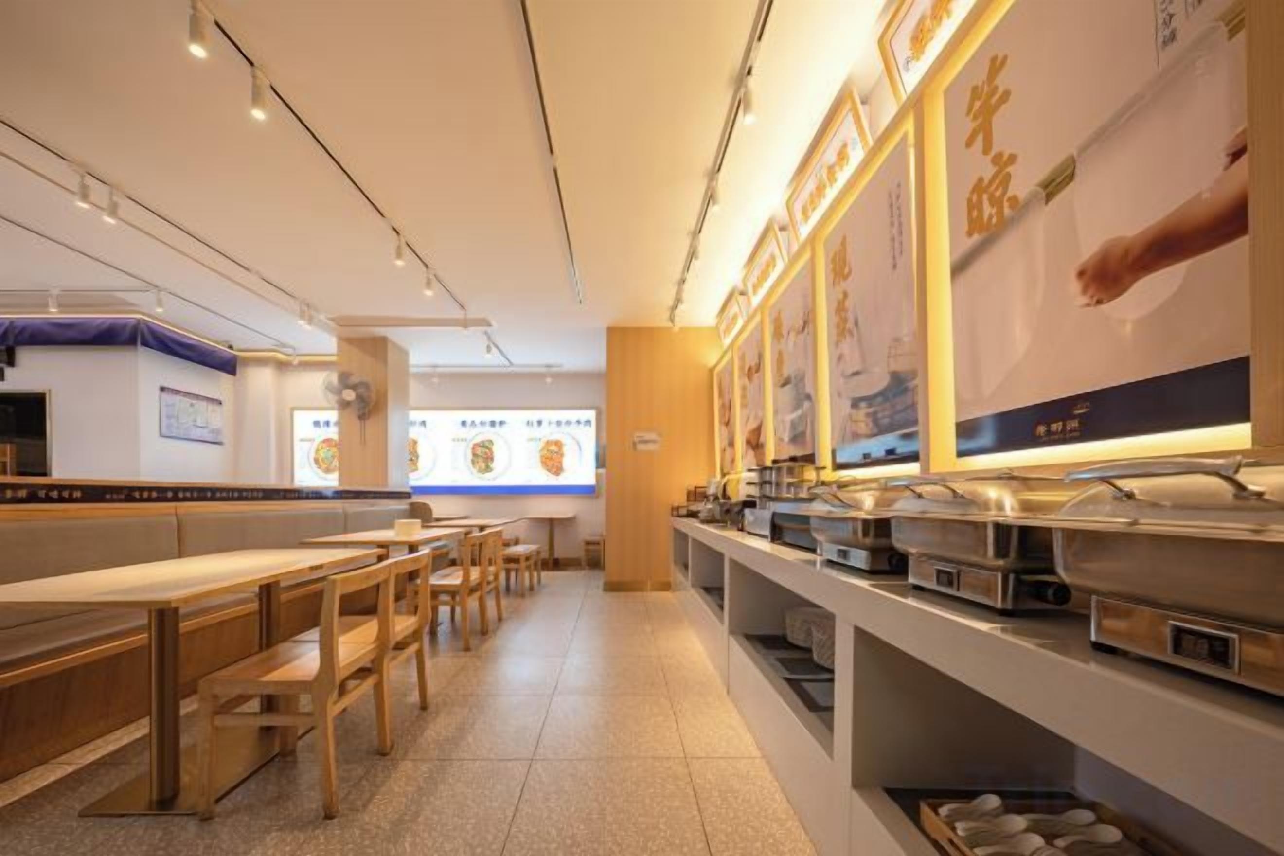 Interior de restaurante com balcão extenso, cadeiras de madeira e área de buffet com recipientes de comida.