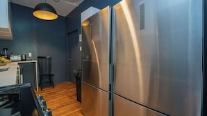 Uma cozinha moderna com eletrodomésticos de aço inoxidável, piso de madeira e uma cadeira preta.