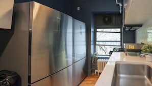 Cozinha moderna com eletrodomésticos de aço inoxidável, bancada branca e janela que permite entrada de luz natural.