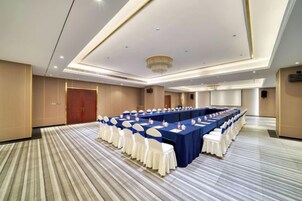 Sala de conferência com uma mesa comprida, cadeiras brancas e um lustre.