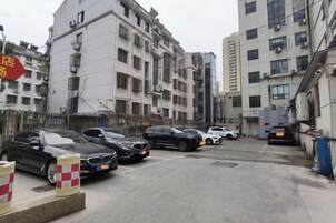 Uma área de estacionamento com vários carros, um edifício com varandas e uma placa vermelha.