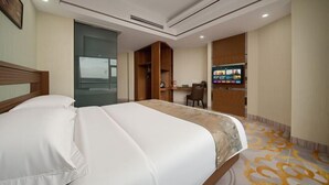 Quarto de hotel com uma cama grande, uma escrivaninha com cadeira, televisão e guarda-roupa.