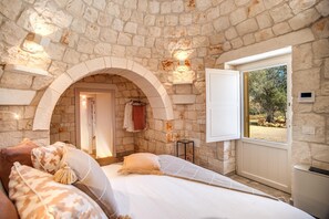 Quarto com paredes de pedra, uma cama, almofadas, um guarda-roupa e uma janela.