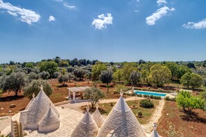 Uma villa com piscina, telhados cônicos e um jardim com oliveiras.