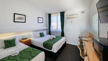 Quarto de hotel com duas camas, uma mesa de cabeceira de madeira, uma pequena mesa com uma televisão e uma janela com cortinas.