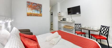 Quarto de hotel com cama, secretária e cadeira, televisão e um quadro na parede.