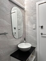 Casa de banho moderna com lavatório branco, bancada preta e um espelho oval grande.