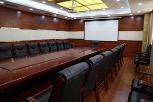 Uma sala de conferência com uma mesa comprida, várias cadeiras, uma tela de projetor e um quadro branco.