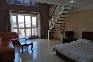Quarto de hotel com cama, sofá, televisão, escada e uma janela grande com cortinas.