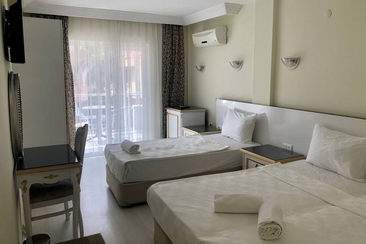 Quarto de hotel com duas camas, uma escrivaninha, uma cadeira, uma televisão e uma janela com cortinas.