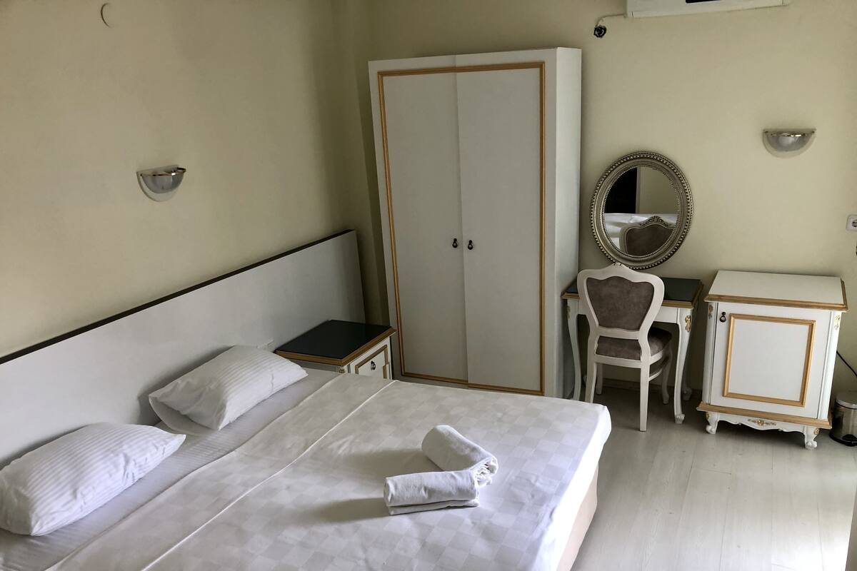 Quarto de hotel com uma cama, uma escrivaninha, uma cadeira, um guarda-roupa e um espelho.