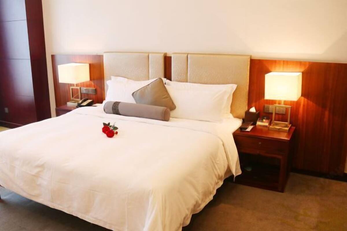Quarto de hotel com uma cama grande, duas mesas de cabeceira e uma cabeceira de madeira.