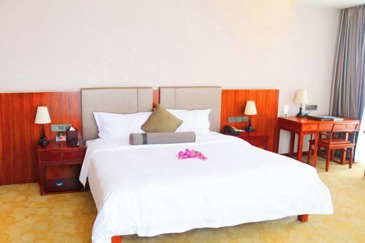 Quarto de hotel com uma cama, duas mesas de cabeceira com luminárias, uma escrivaninha com cadeira e uma cortina na janela.