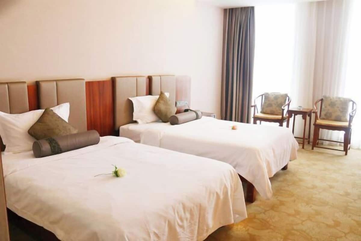 Quarto de hotel com duas camas, uma cadeira e uma mesa pequena.
