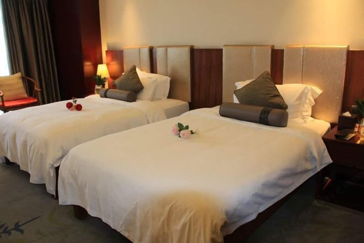 Quarto de hotel com duas camas, cada uma com cabeceira de madeira, roupa de cama branca e almofadas decorativas.