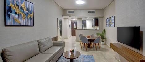 Uma sala de estar moderna com um sofá, uma mesa de centro, uma área de jantar com cadeiras e uma mesa, uma TV de tela plana e obras de arte nas paredes.