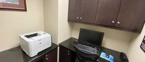 Um pequeno espaço de escritório com uma mesa, impressora, laptop e telefone.