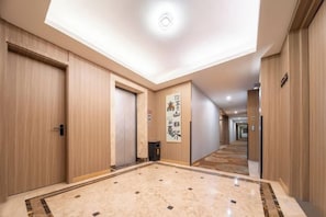 Corredor de hotel com portas de madeira, chão de mármore e uma placa na parede.