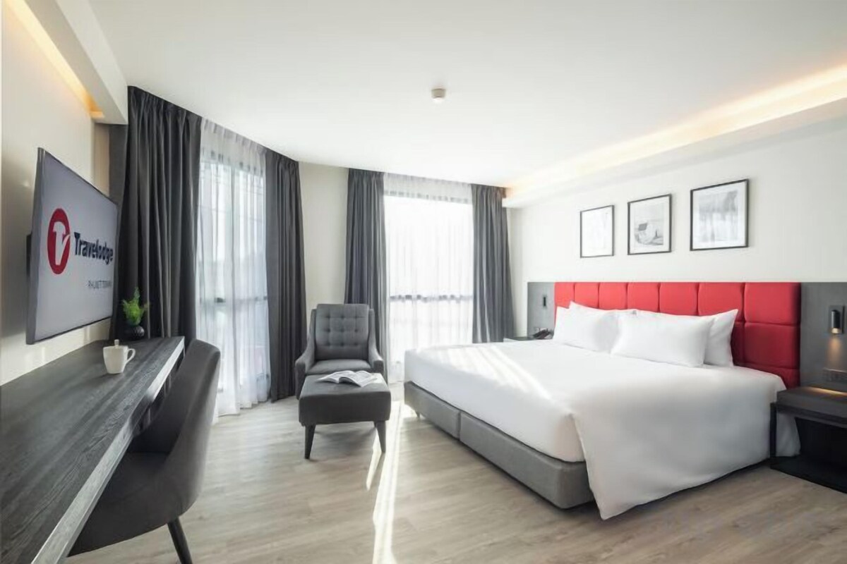 Quarto de hotel com cama, escrivaninha, cadeira, televisão e janela com cortinas.