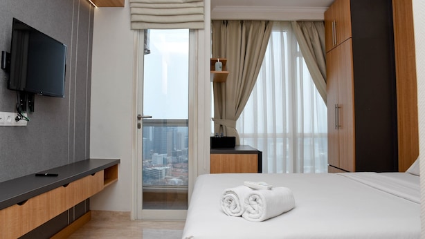 Quarto de hotel com cama, televisão fixada na parede, secretária de madeira e vista para a cidade pela janela.