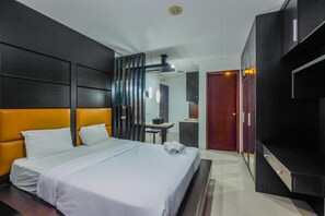 Quarto de hotel com uma cama grande, uma escrivaninha, um espelho e uma televisão.