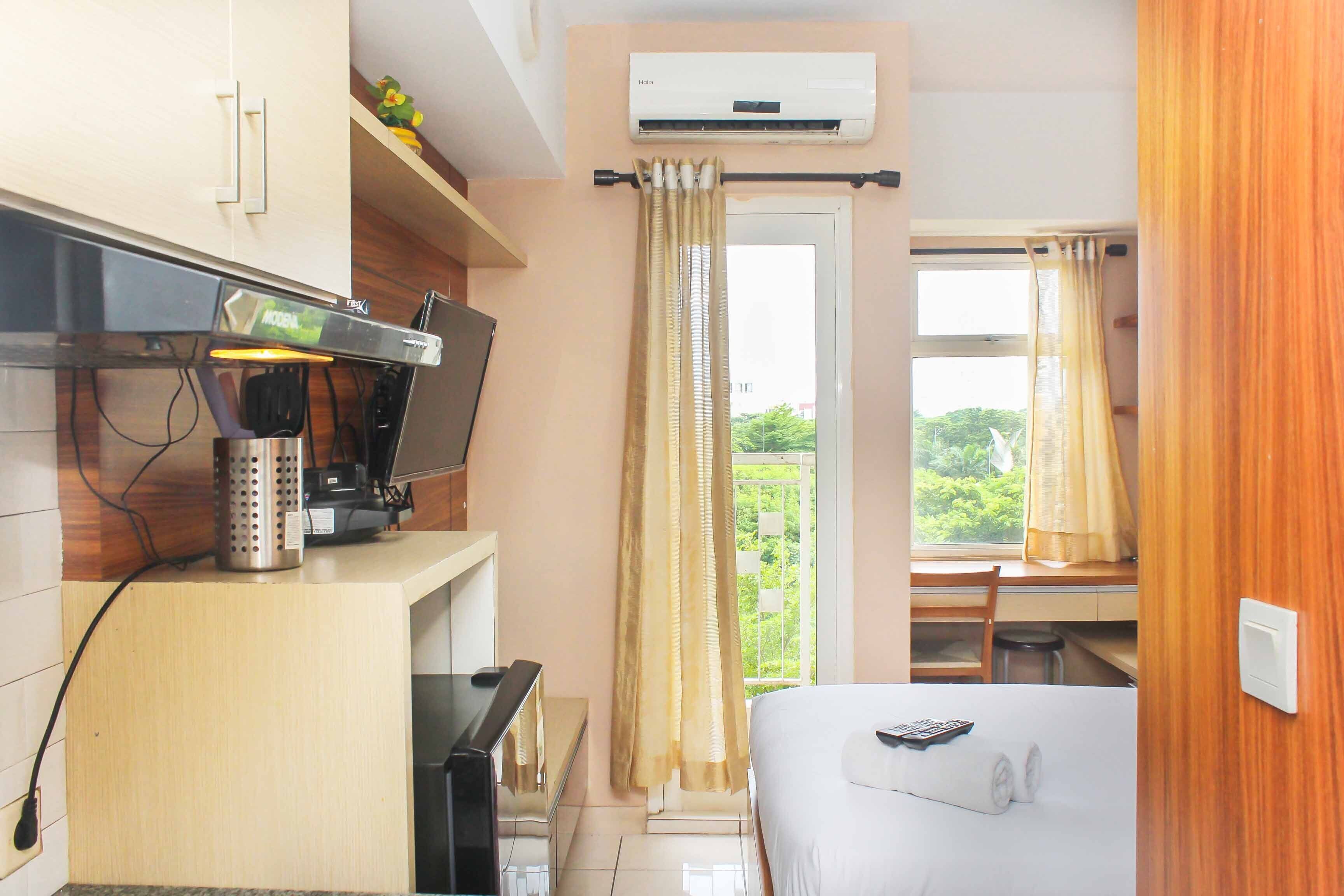 Quarto de hotel compacto com cozinha compacta, uma cama, escrivaninha com computador e janela com cortinas.