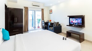 Quarto de hotel com uma cama grande, uma escrivaninha com cadeira, televisão na parede e um guarda-roupa.