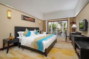 Quarto de hotel com cama, escrivaninha, televisão e varanda com vista para palmeiras.