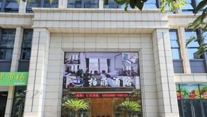 Entrada de hotel com uma placa grande, plantas em vasos e fachada revestida de azulejos.